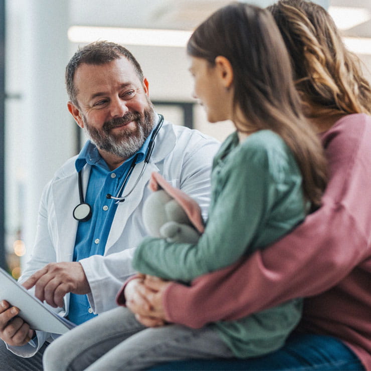 a smiling physician talks to his young patient and her mother