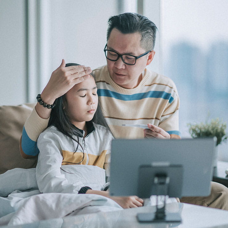 a father feels his daughter's forehead for fever during a virtual urgent care appointment on a ...