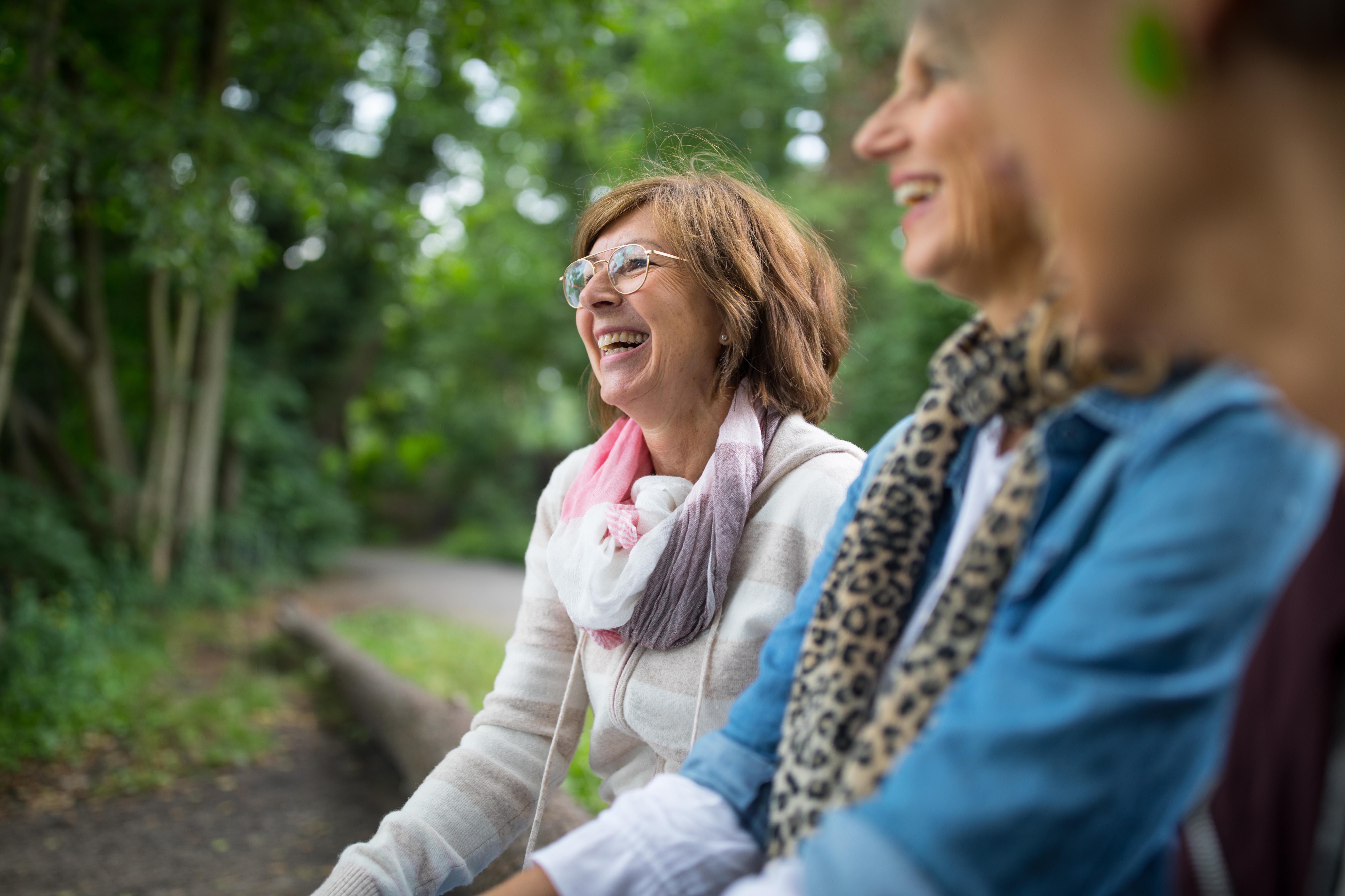 A small group of happy women looking away while sitting at a lakeshore.